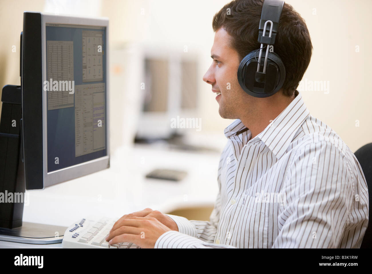 Man wearing headphones in computer room typing and smiling Stock Photo ...