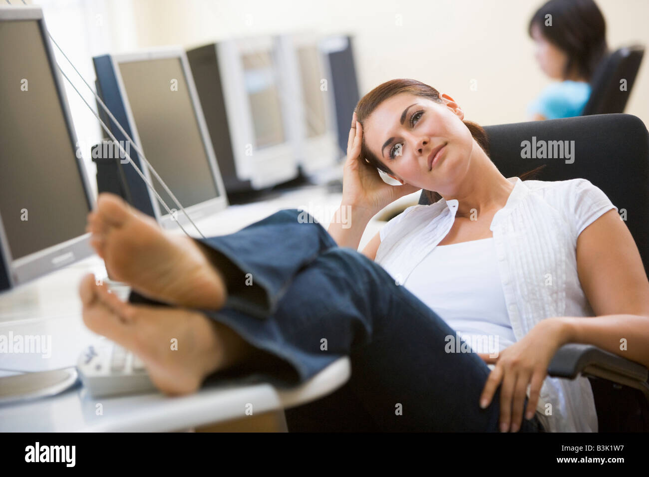 Woman in computer room with feet up thinking Stock Photo - Alamy