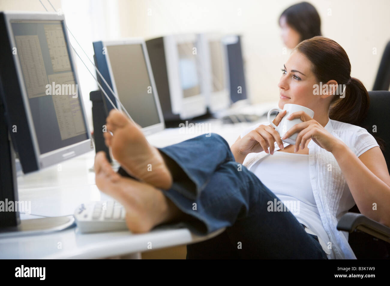 Woman in computer room with feet up drinking coffee Stock Photo - Alamy