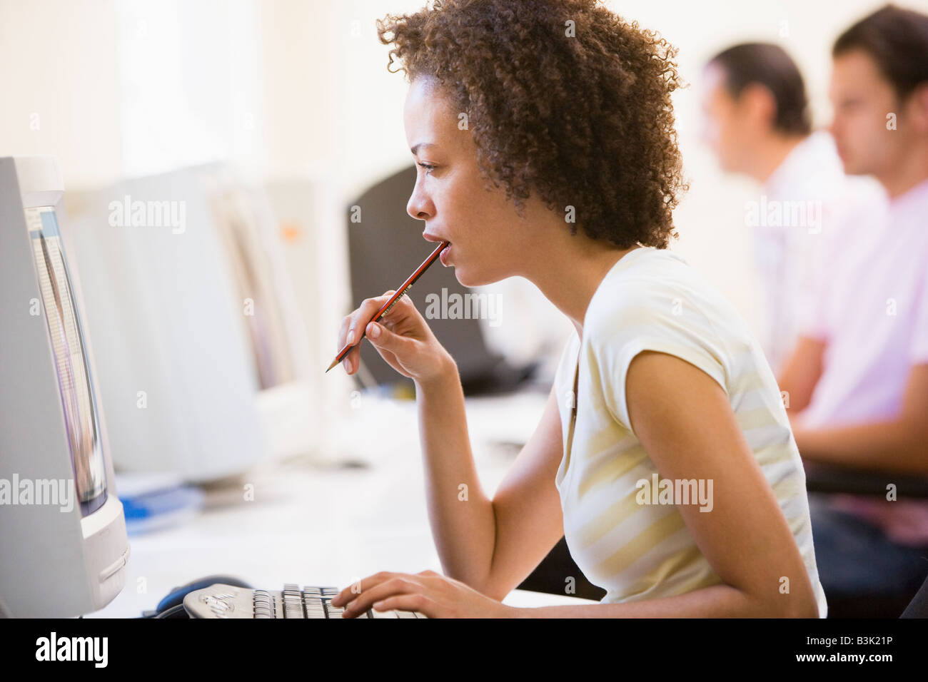 Woman in computer room looking at monitor and thinking Stock Photo - Alamy
