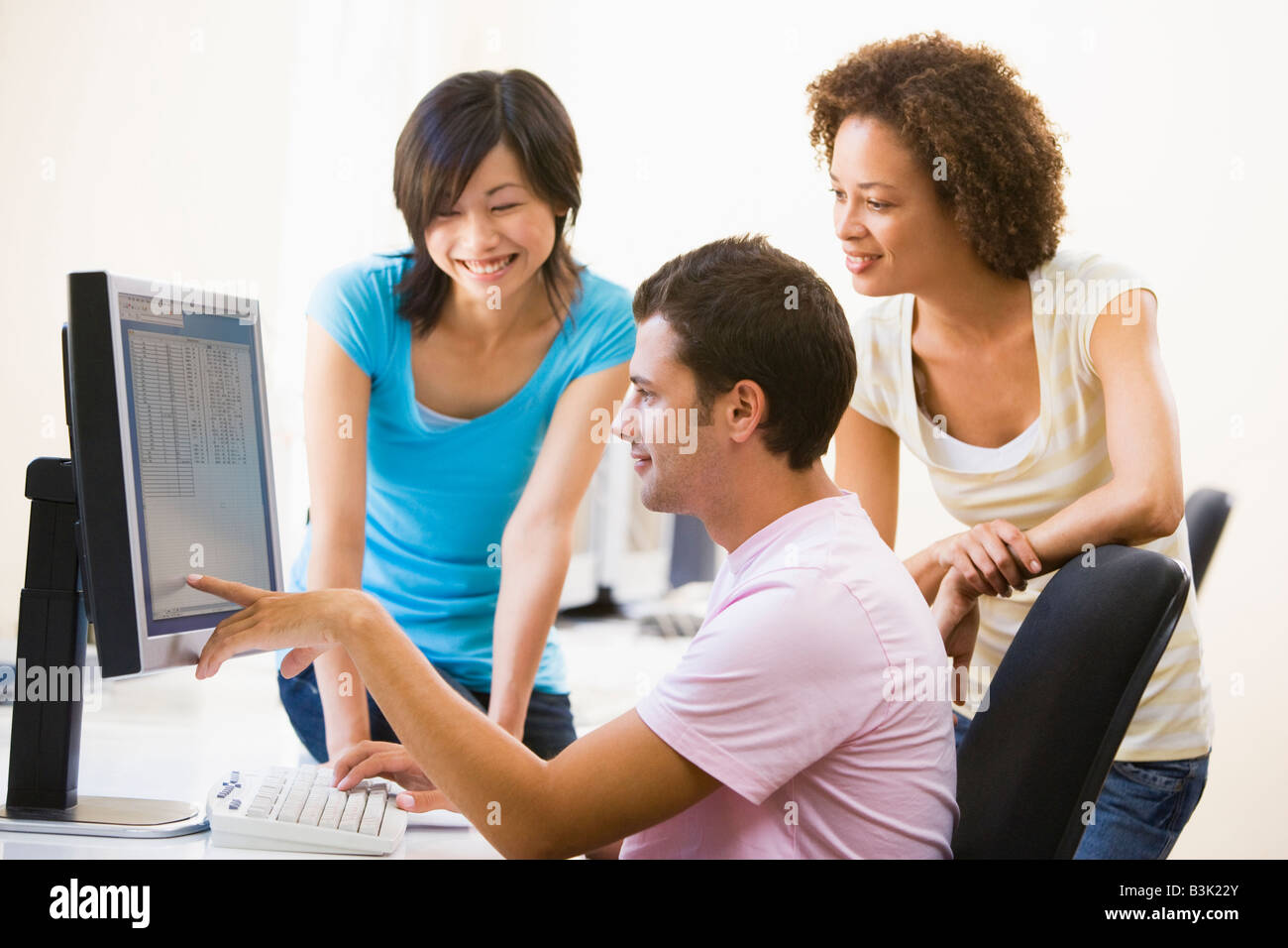 Three people in computer room pointing at monitor and smiling Stock ...