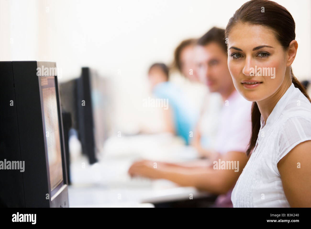 Woman sitting in computer room with people in background Stock Photo ...