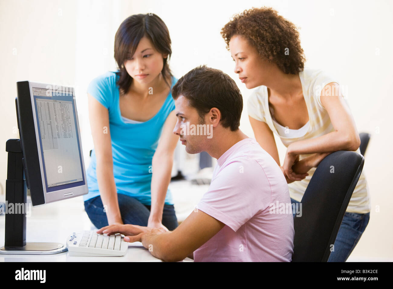 Three people sitting in computer room looking at monitor Stock Photo ...