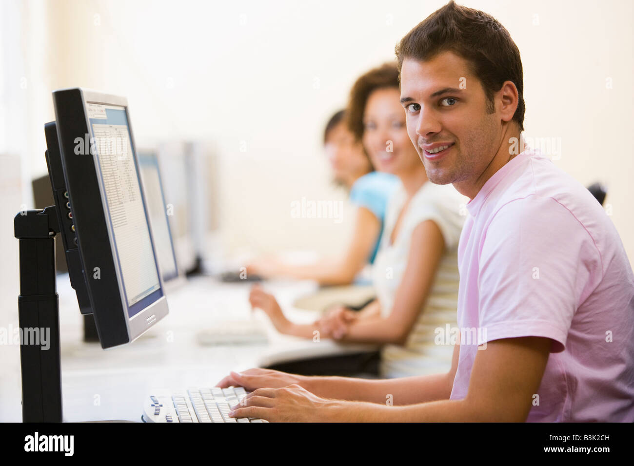 Three people sitting in computer room typing and smiling Stock Photo ...