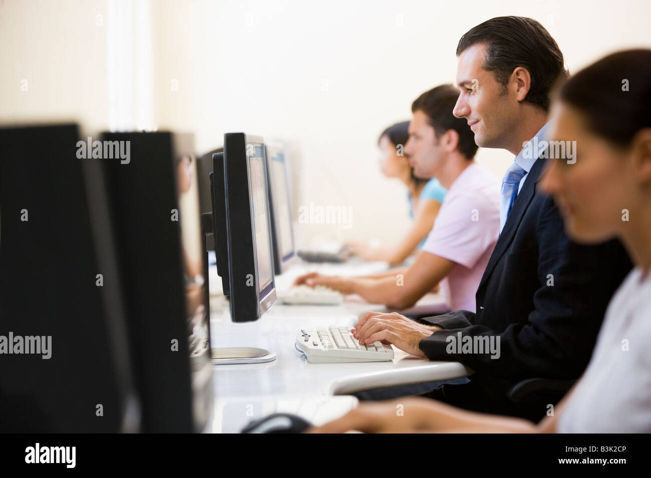 Four people sitting in computer room typing with one man in a suit ...