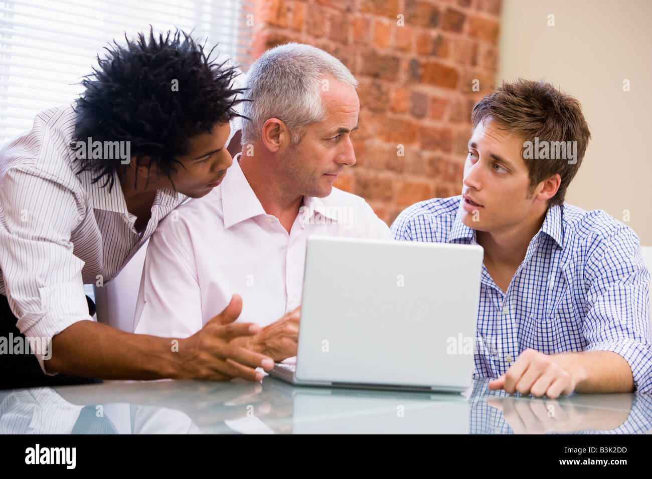 Three businessmen in office with laptop talking Stock Photo - Alamy