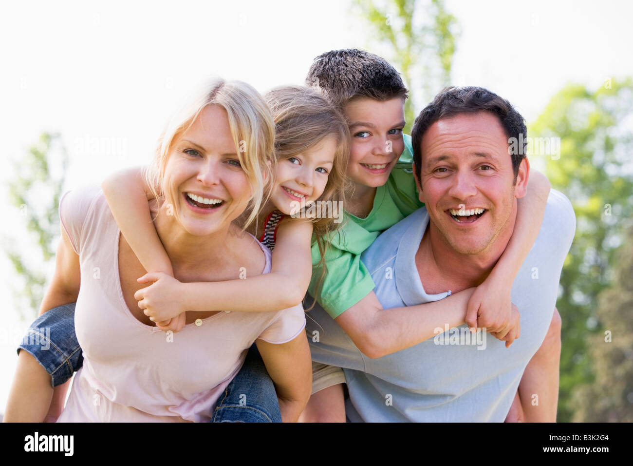 Couple giving two young children piggyback rides smiling Stock Photo ...