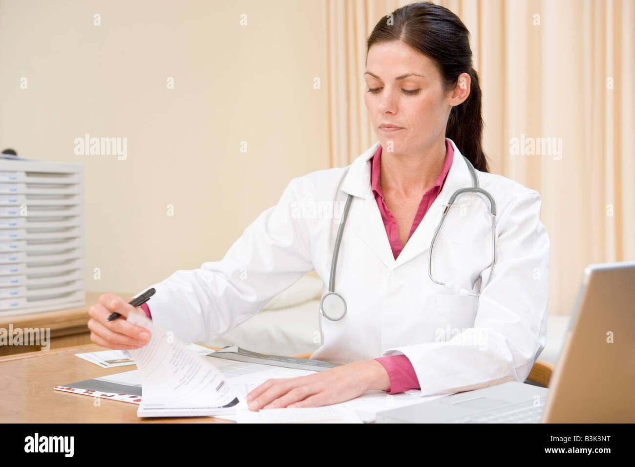 Doctor with laptop writing in doctor's office smiling Stock Photo - Alamy