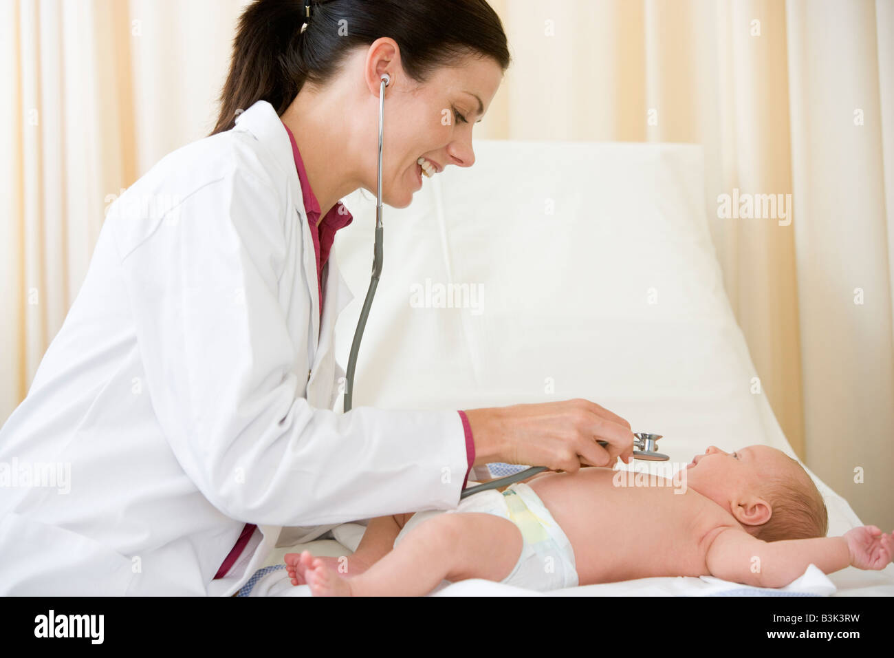 Doctor giving checkup with stethoscope to baby in exam room smiling ...