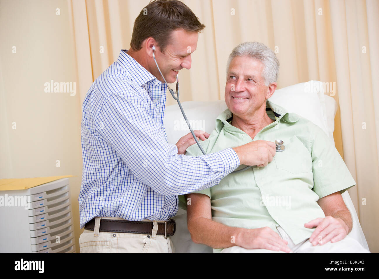 Doctor giving man checkup with stethoscope in exam room smiling Stock ...