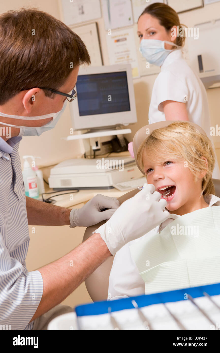 Dentist and assistant in exam room with young boy in chair Stock Photo ...