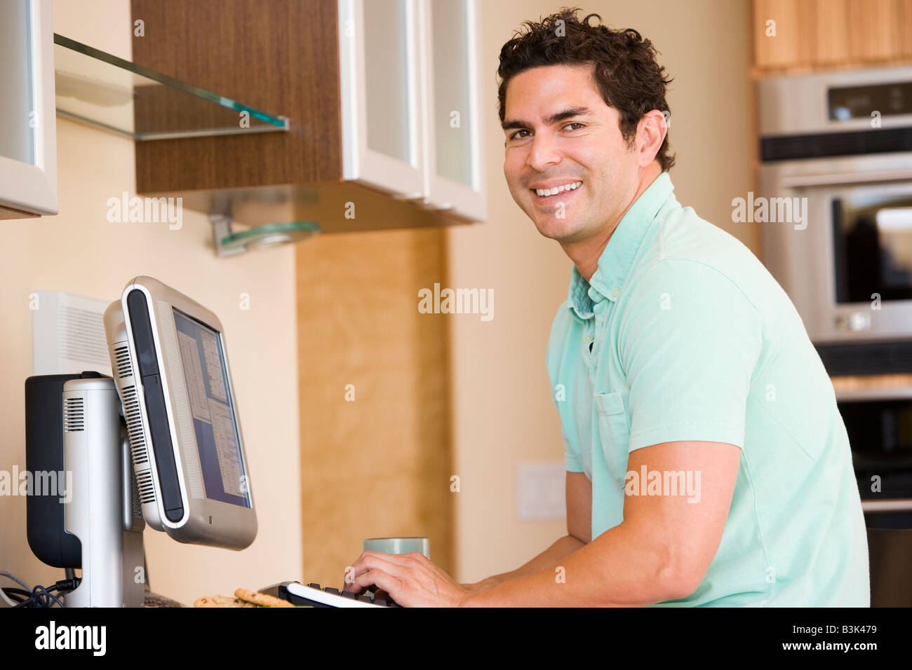 Man in kitchen using computer and smiling Stock Photo - Alamy