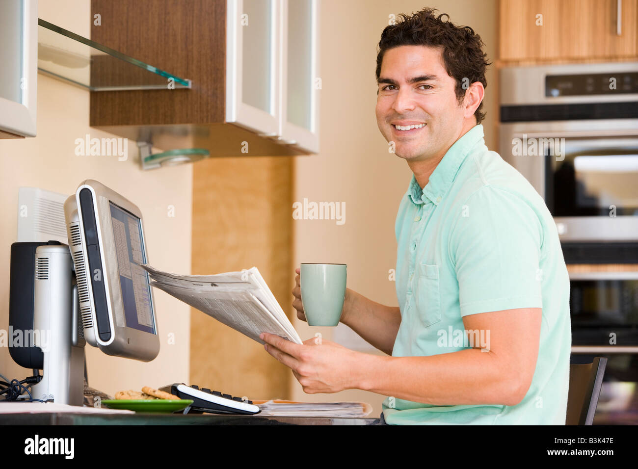 Man in kitchen with computer holding newspaper and coffee smiling Stock ...