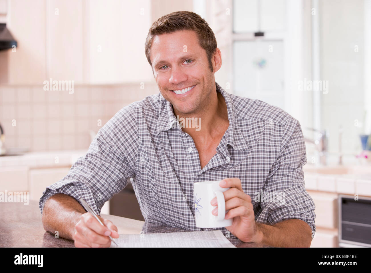 Man in kitchen reading newspaper and smiling Stock Photo - Alamy