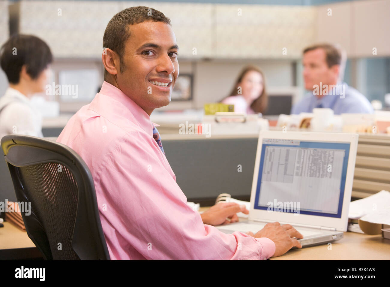 Businessman in cubicle with laptop smiling Stock Photo - Alamy