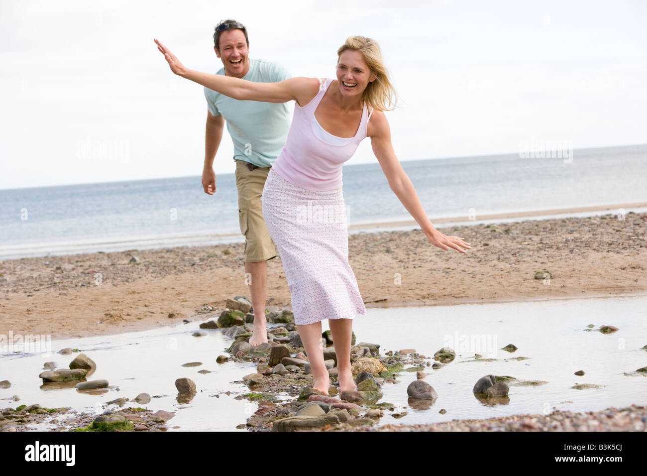 Couple at the beach walking on stones and smiling Stock Photo - Alamy