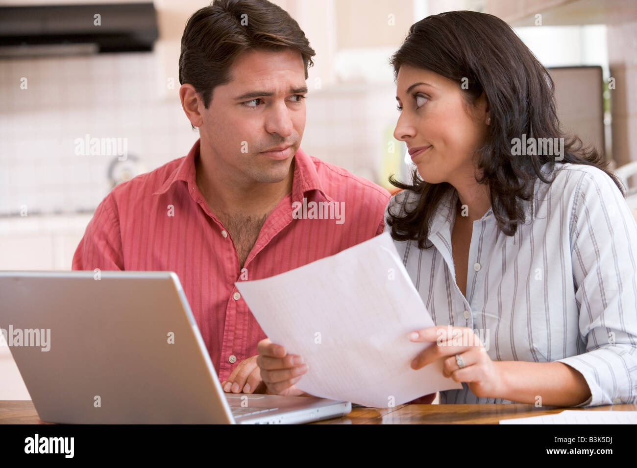 Couple in kitchen with paperwork using laptop looking unhappy Stock ...