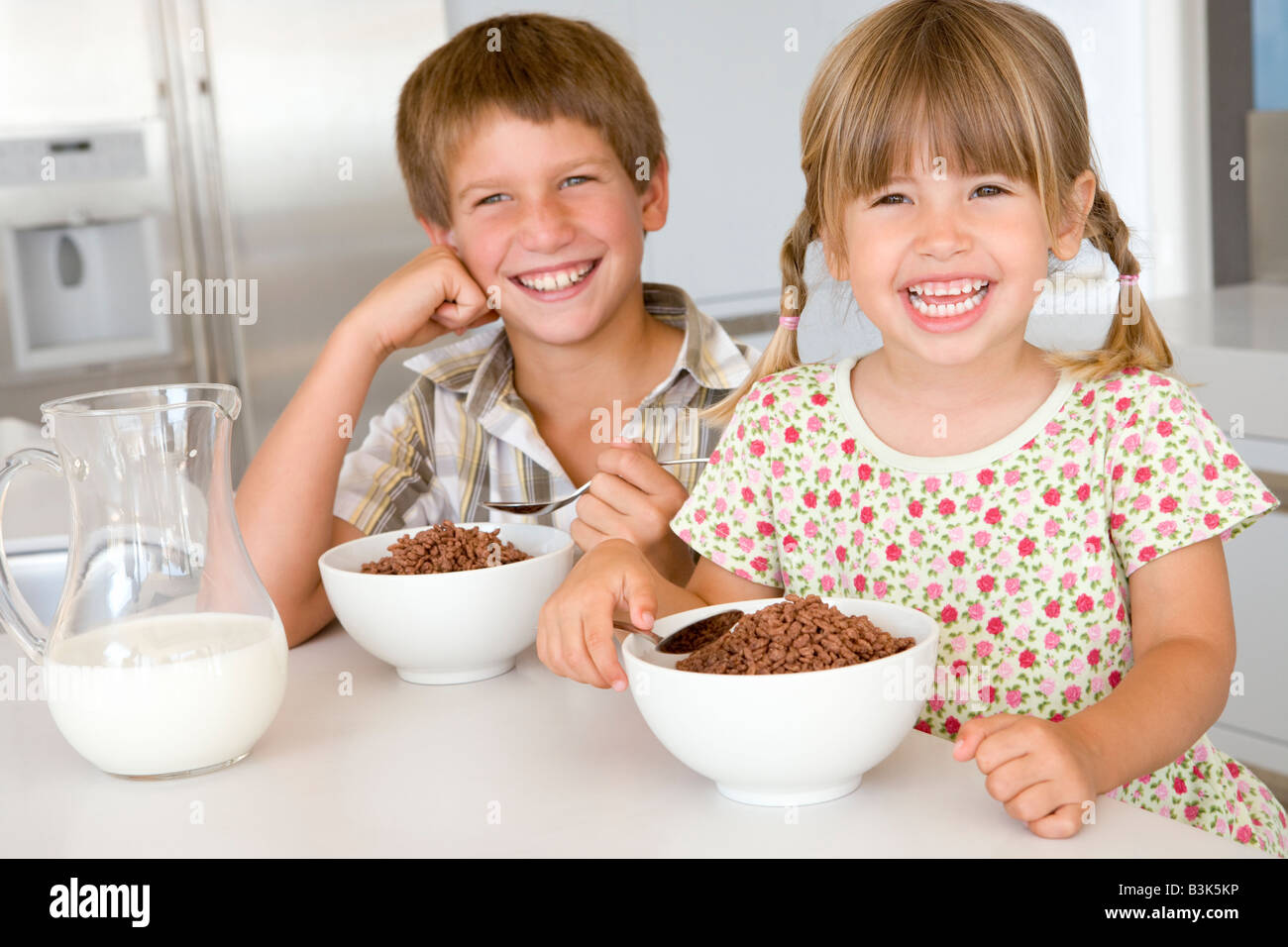 Two young children in kitchen eating cereal smiling Stock Photo - Alamy