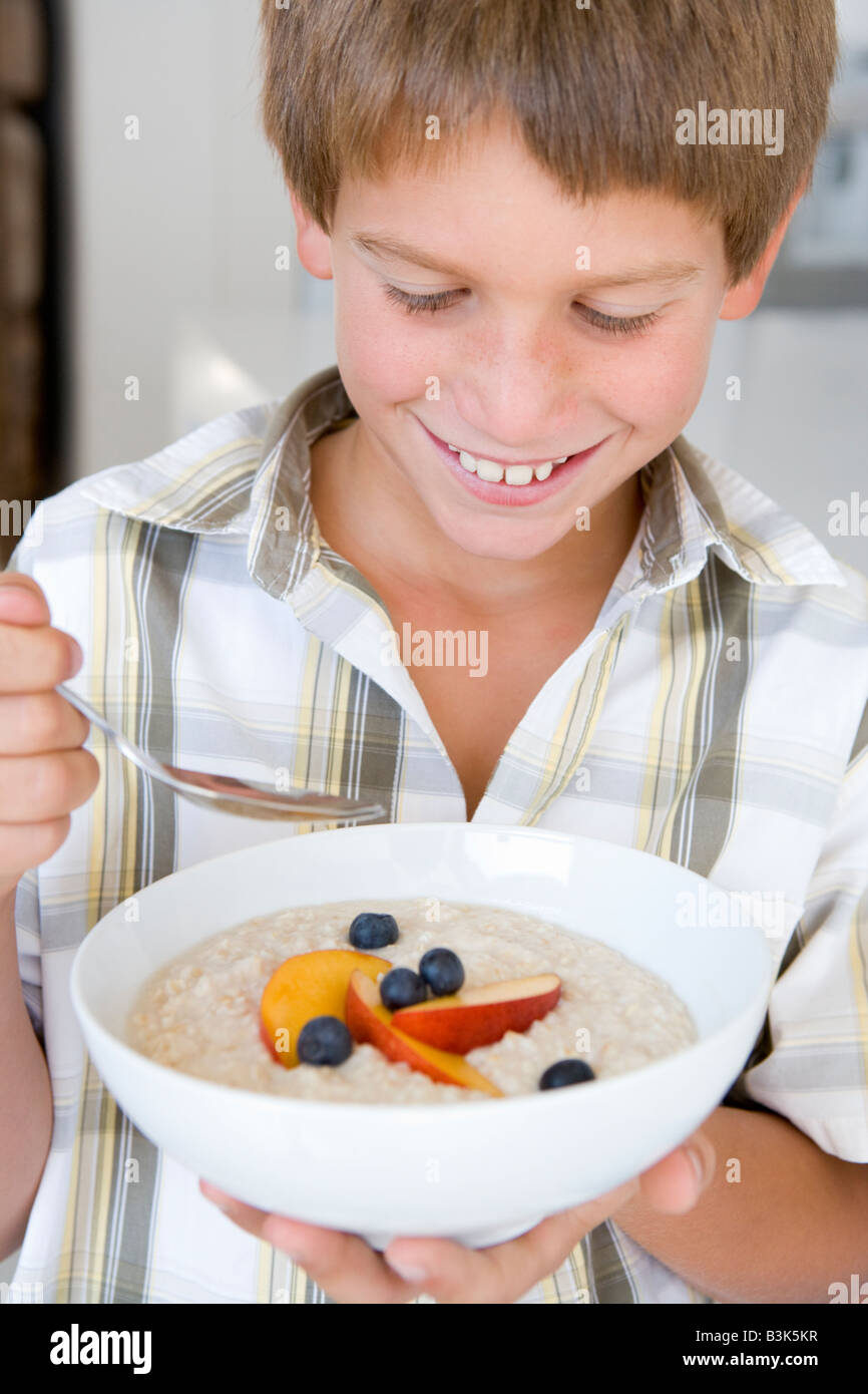Young boy in kitchen eating oatmeal with fruit smiling Stock Photo - Alamy
