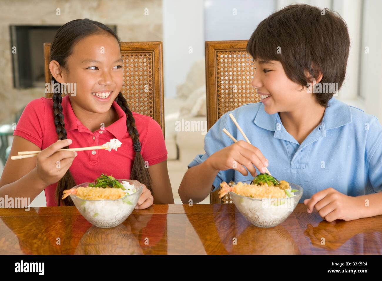 Two young children eating Chinese food in dining room smiling Stock ...