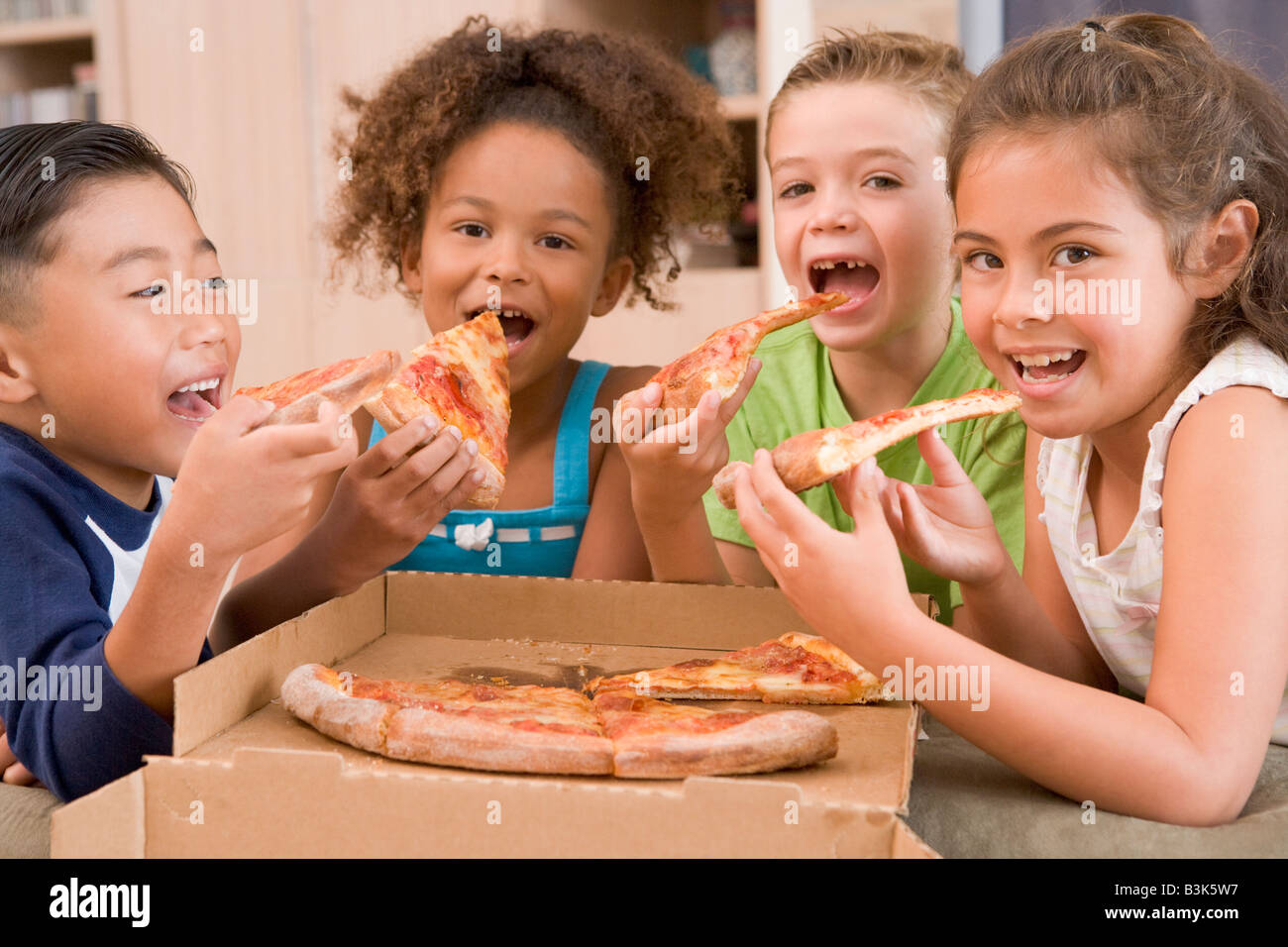 Four young children indoors eating pizza smiling Stock Photo - Alamy