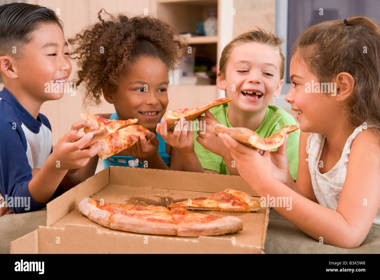 Four young children indoors eating pizza smiling Stock Photo - Alamy