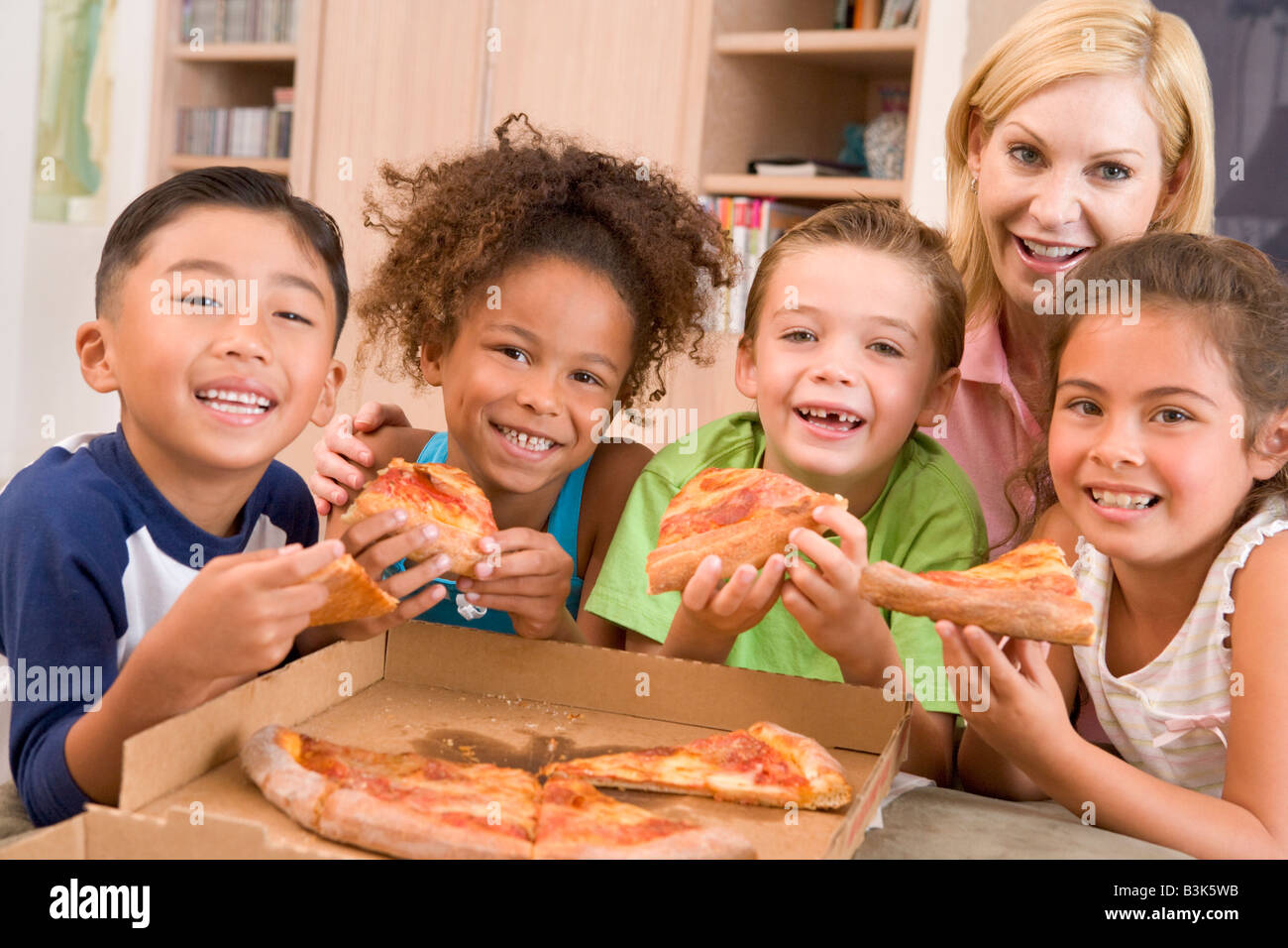 Four young children indoors with woman eating pizza smiling Stock Photo ...