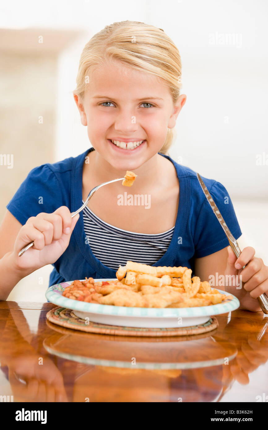 Young girl indoors eating fish and chips smiling Stock Photo - Alamy