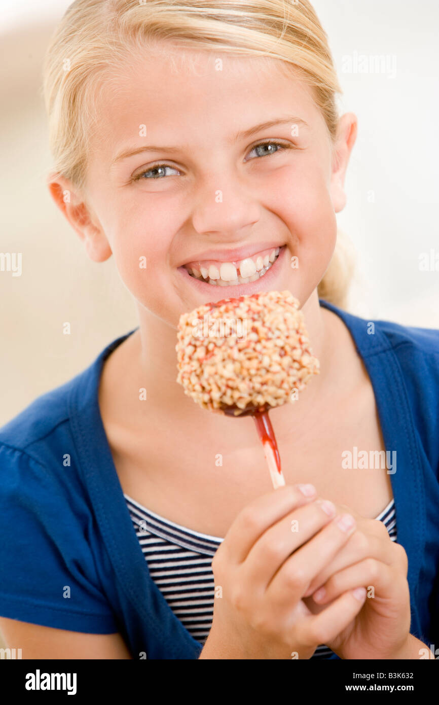Young girl indoors eating candy apple smiling Stock Photo - Alamy