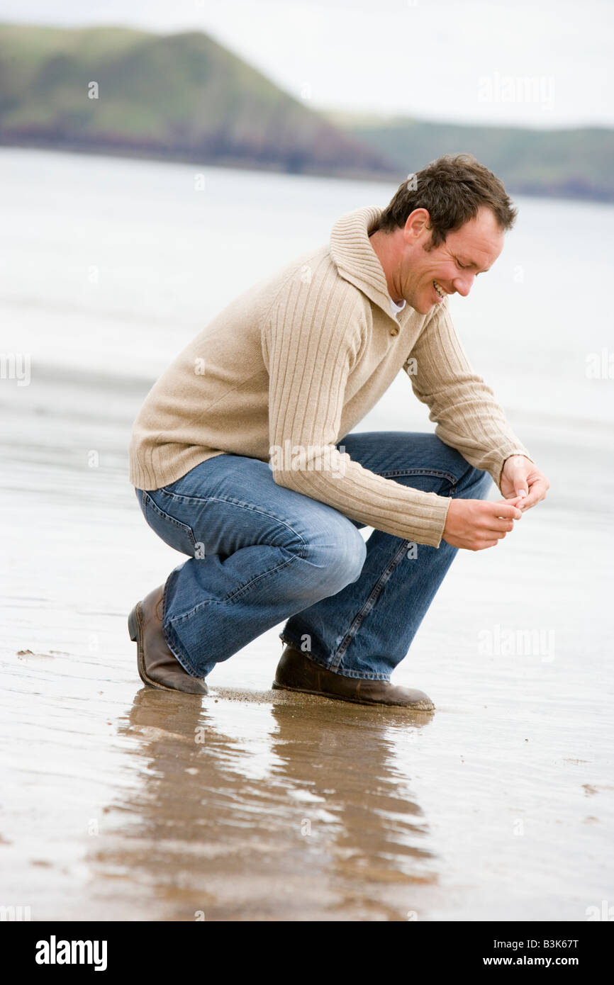 Man crouching on beach smiling Stock Photo - Alamy