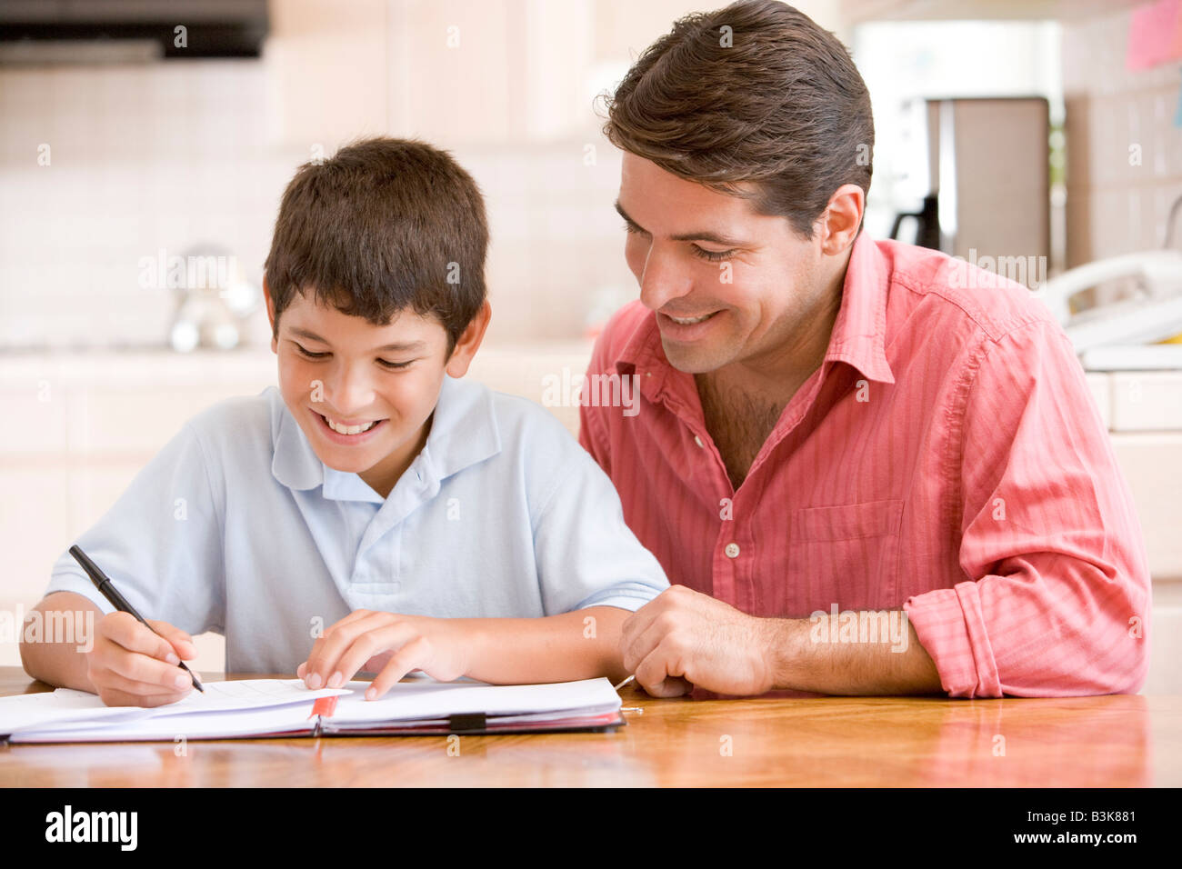 Man helping young boy in kitchen doing homework and smiling Stock Photo ...
