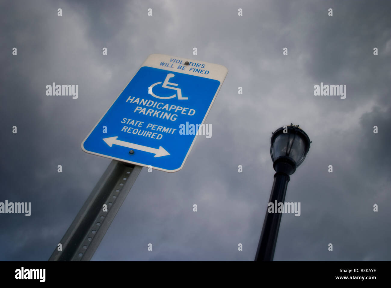 Traffic sign on a metal pole next to a lamppost reading HANDICAPPED ...
