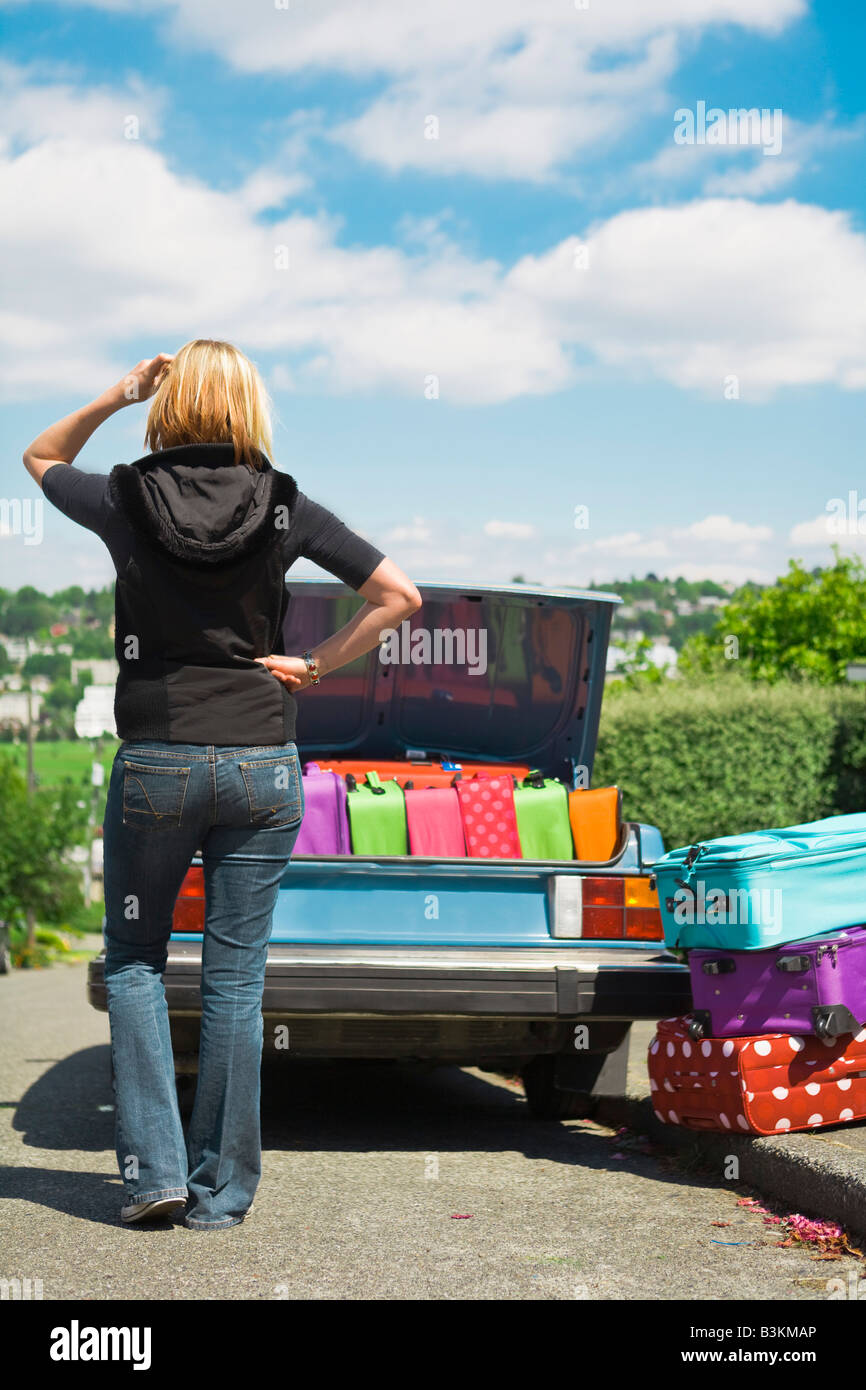 Confused woman loading car trunk with colorful suitcases Stock Photo ...