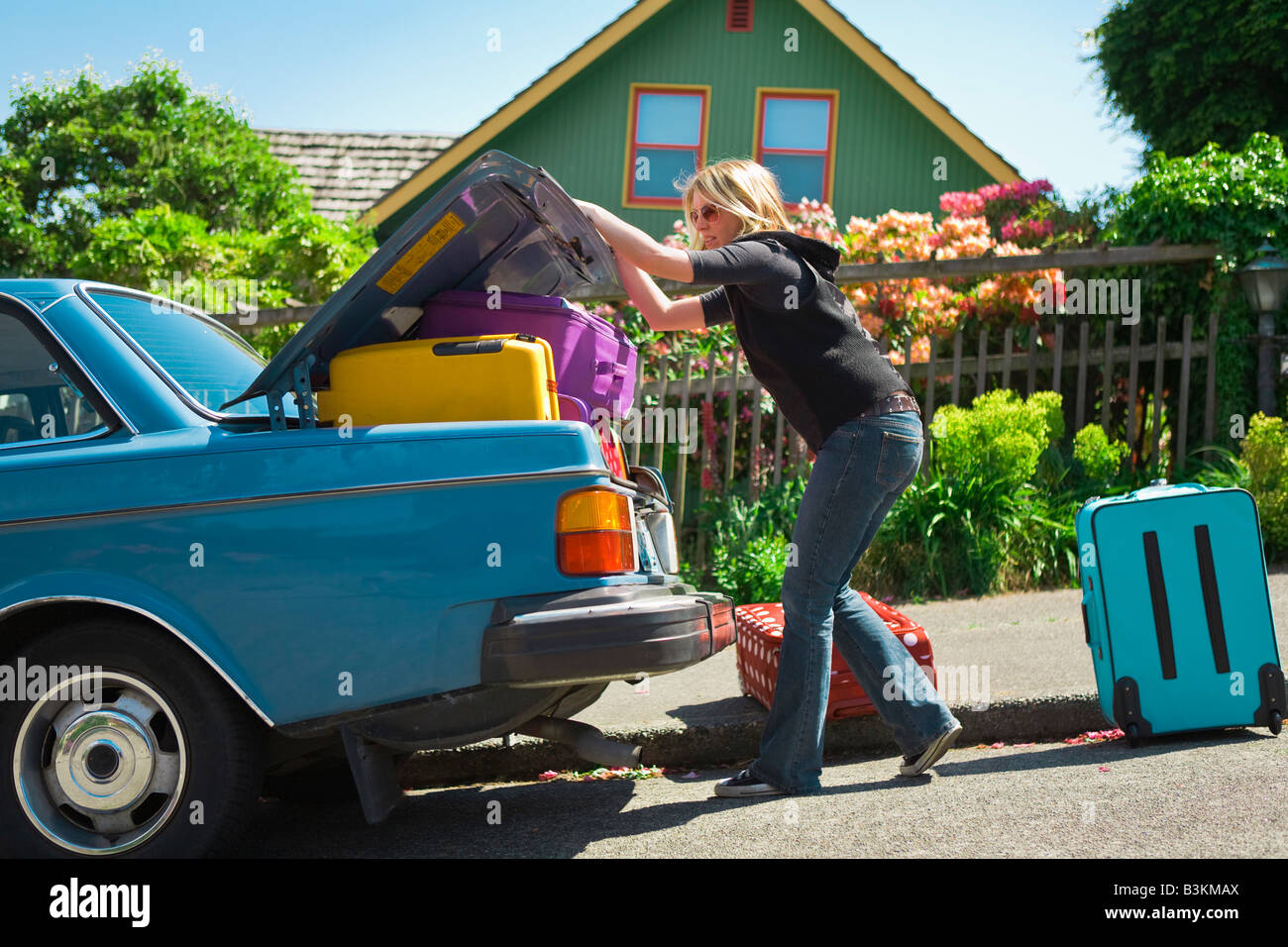 Woman loading car trunk with colorful suitcases Stock Photo - Alamy