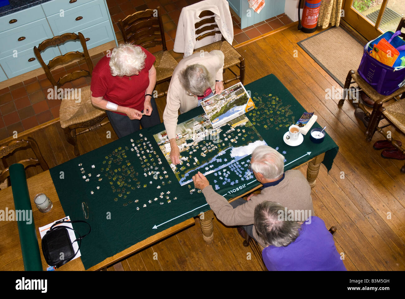 Overhead shot of 4 elderly people doing a large jig-saw puzzle on a ...
