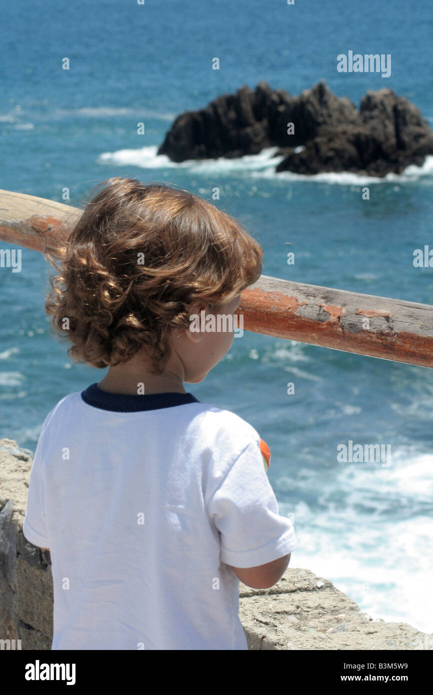 A young boy standing at a railing looking out at the ocean Stock Photo ...