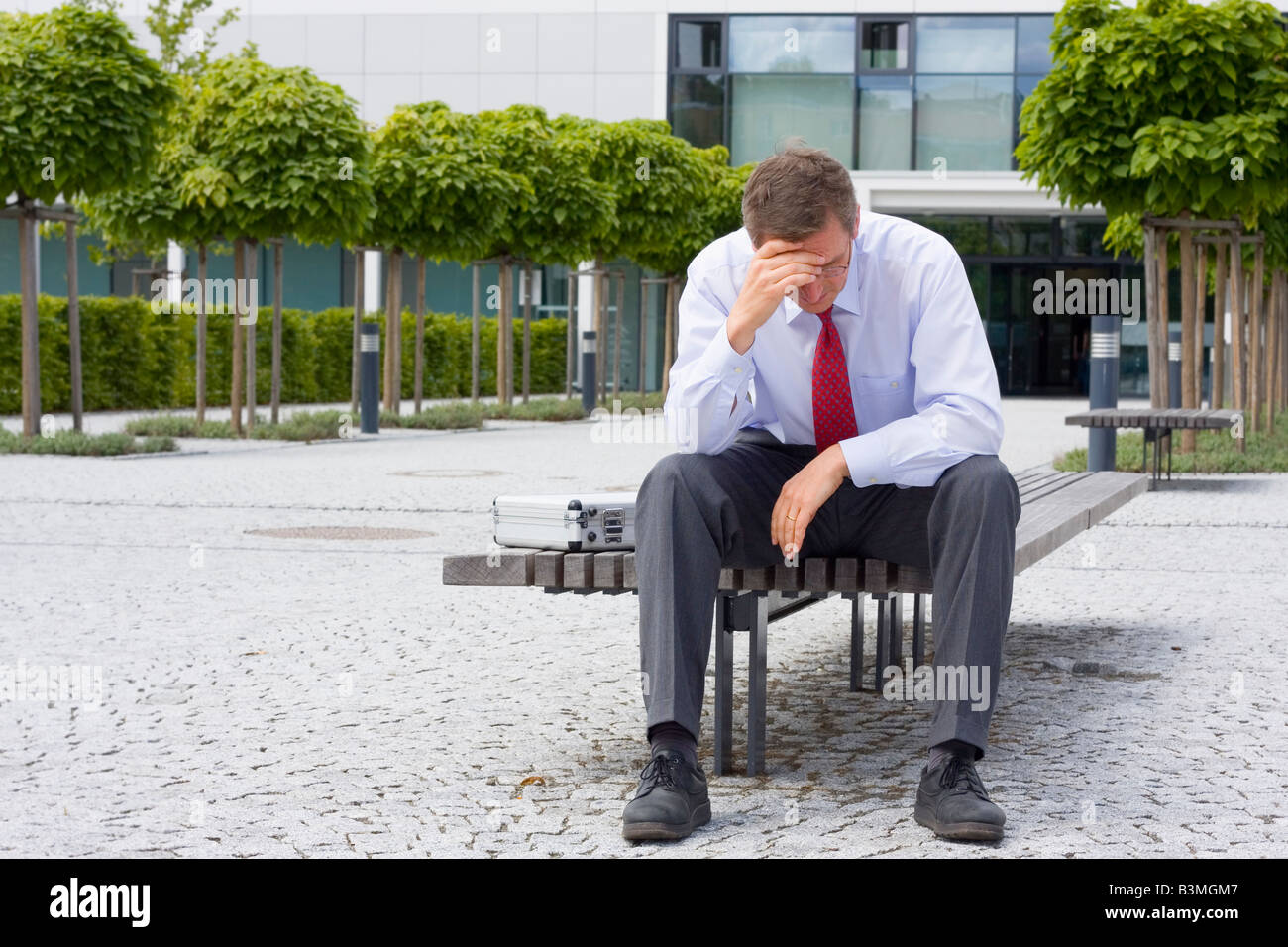 Sorrowful businessman sitting on a bench in front of an office building ...