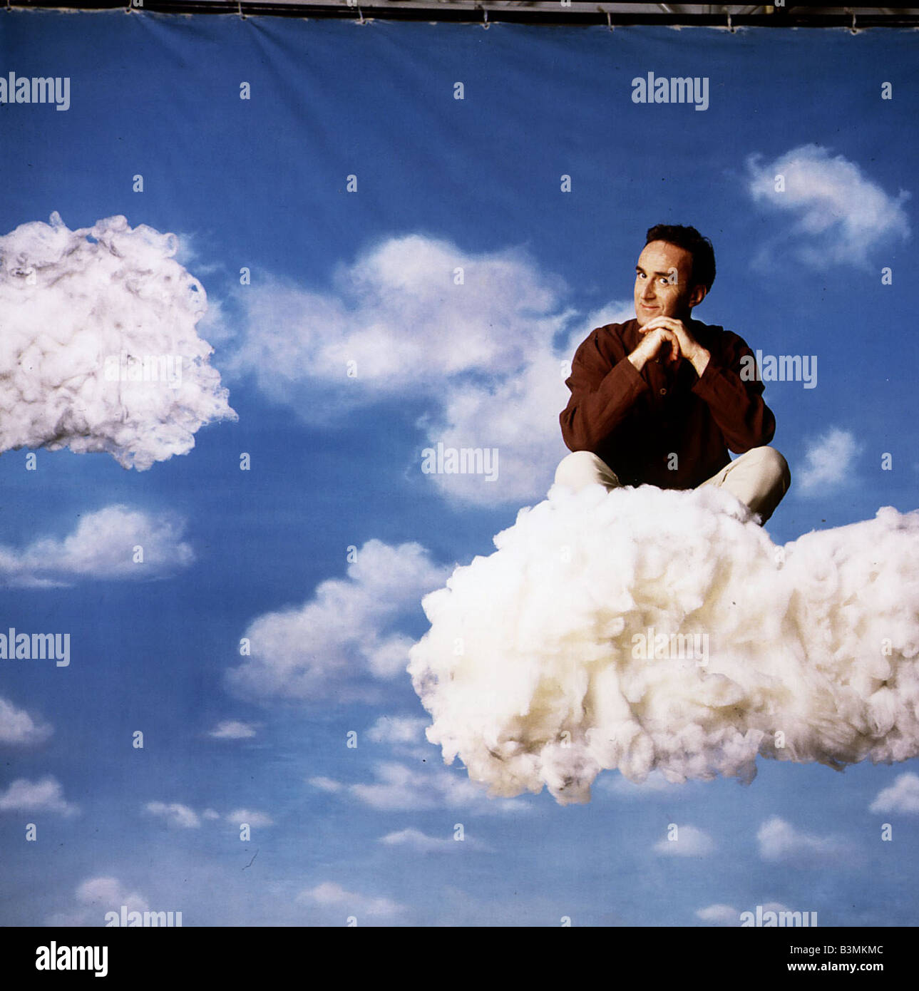 Angus Deayton TV presenter sitting on cloud in sky background back drop ...