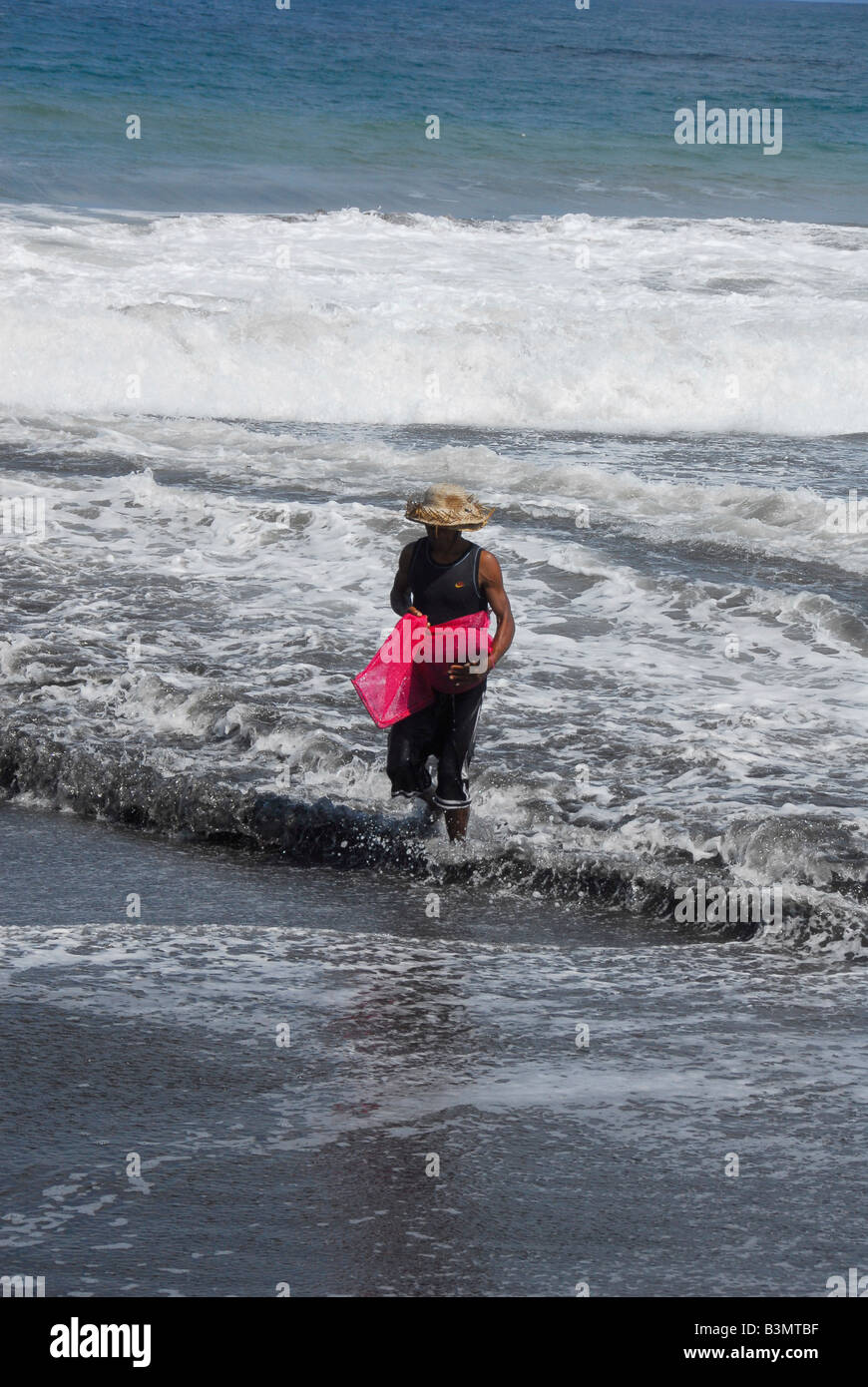 man collecting pebbles as the surf goes in and out,kusamba ,bali ...