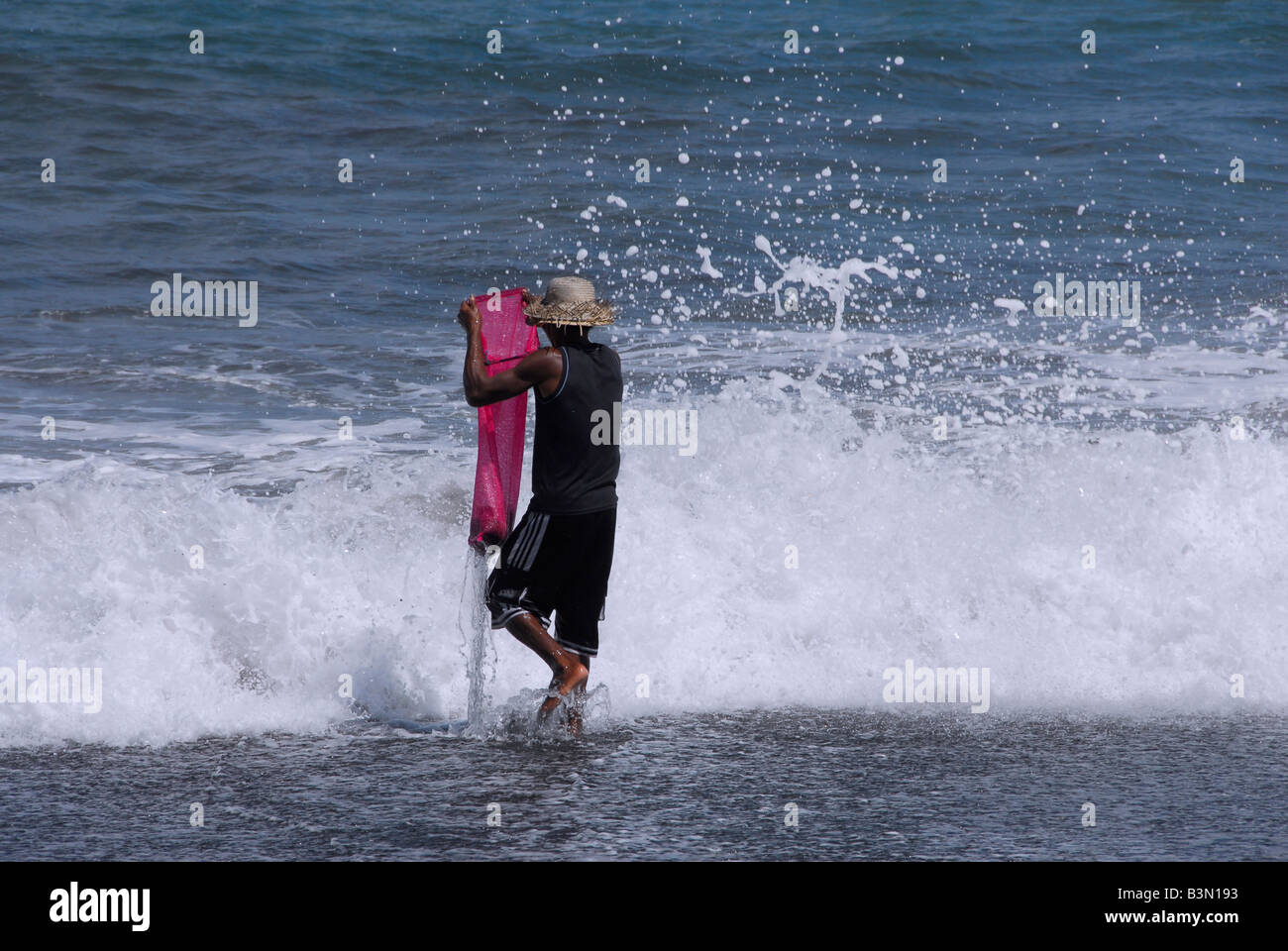 man collecting pebbles as the surf goes in and out,kusamba ,bali ...