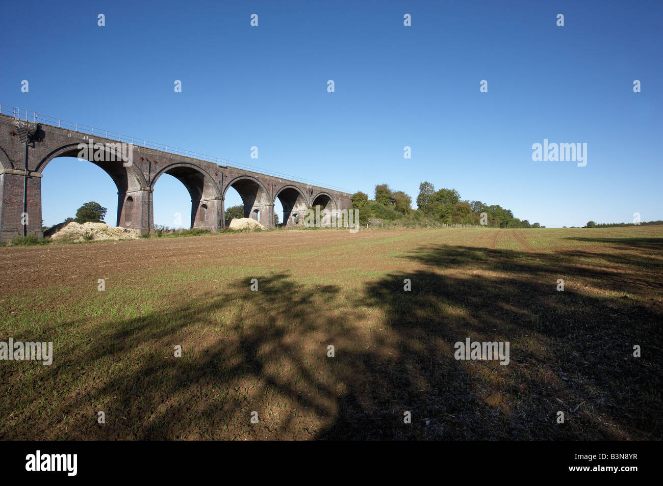Victorian brick railway viaduct running through a field on a blue sky ...