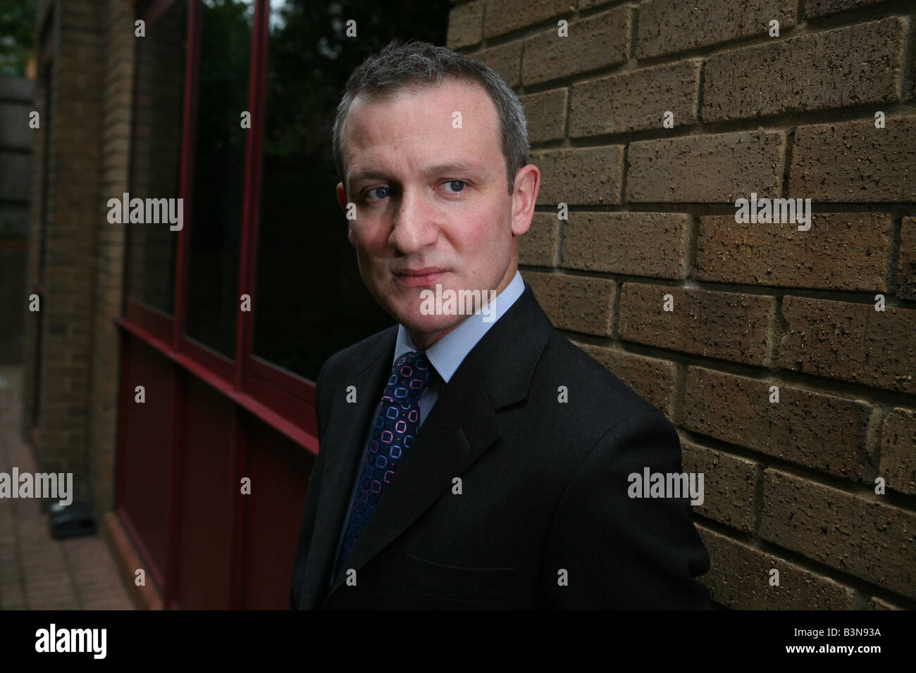 a portrait of a solicitor standing outside his office next to a brick ...