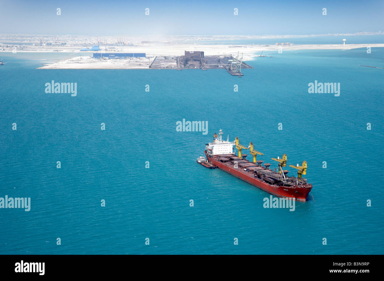 A cargo ship lies at anchor of the coast of Bahrain in rich blue sea ...