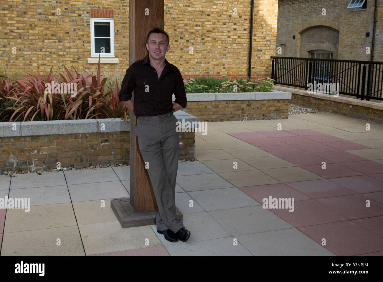 Portrait of a young handsome man leaning up against a beam waring ...