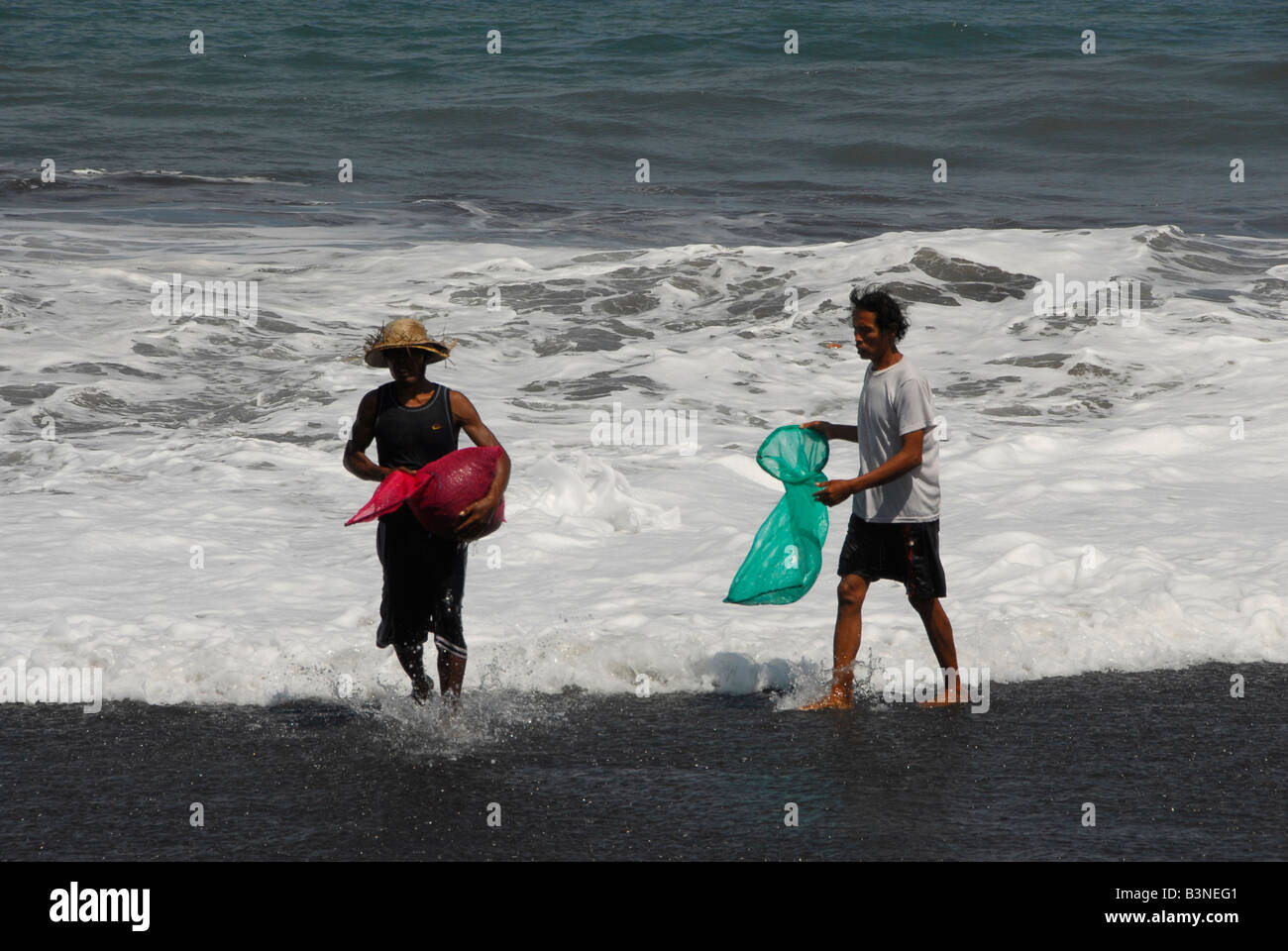 men collecting pebbles as the surf goes in and out,kusamba ,bali ...
