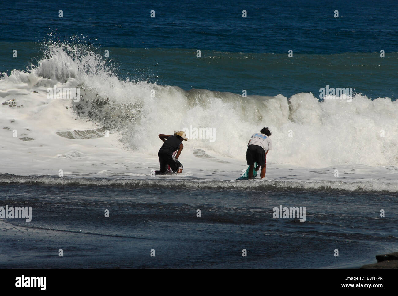 men collecting pebbles as the surf goes in and out,kusamba ,bali ...