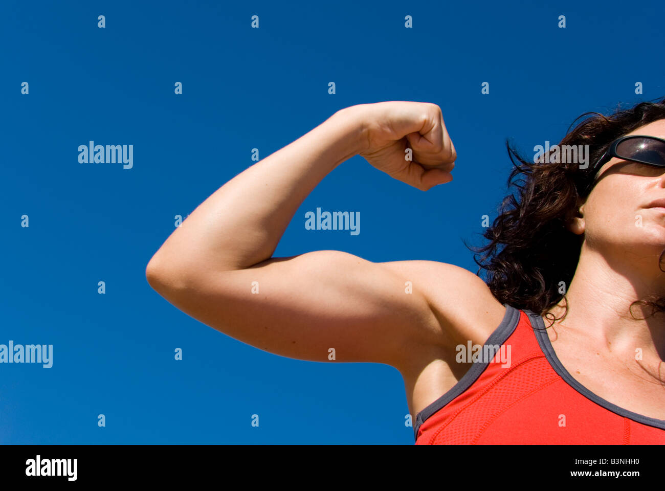 Model Released sporty female flexing biceps against a clear blue sky ...