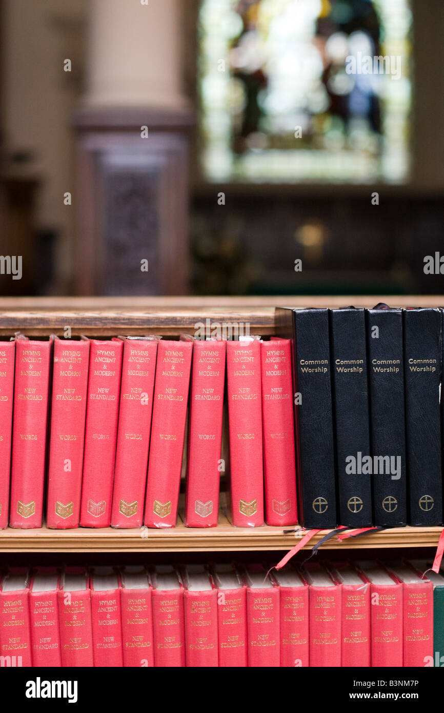 Red hymn books and bibles stacked on a shelf against pews in a church ...