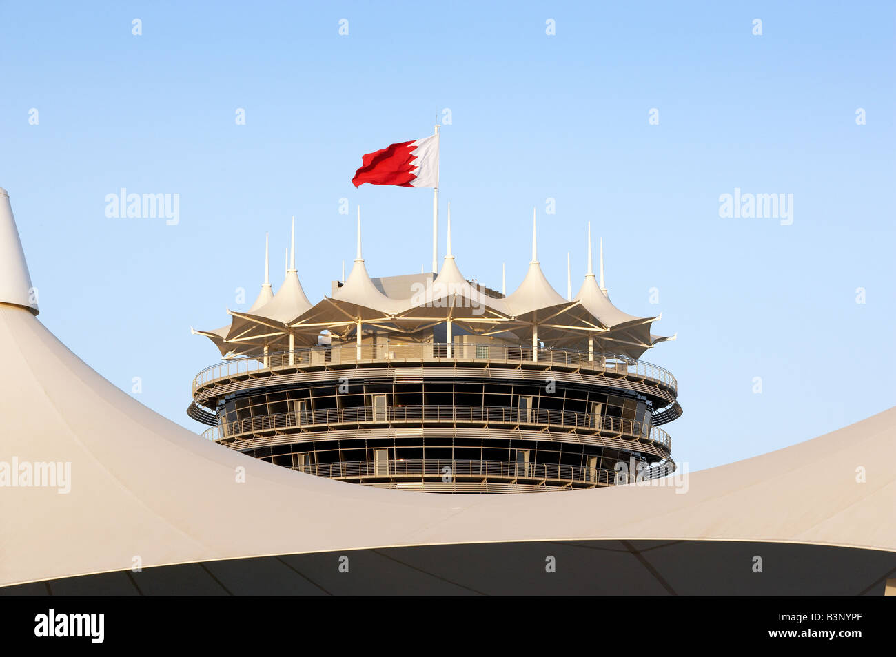 The top of the Sakhir Tower with the Bahrain flag flying in a blue sky ...