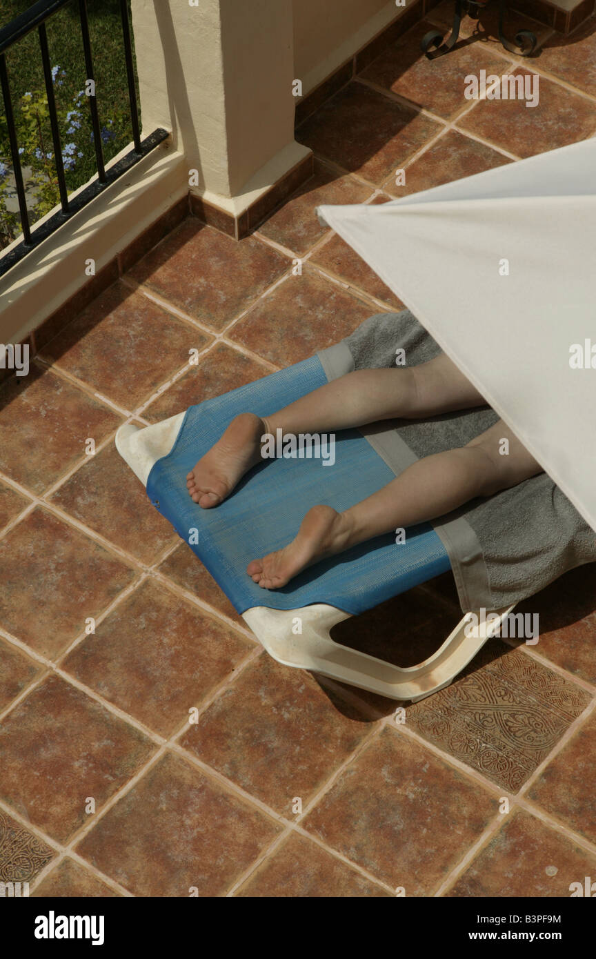 female laid in shade tanning only legs and feet on roof terrace viewed ...